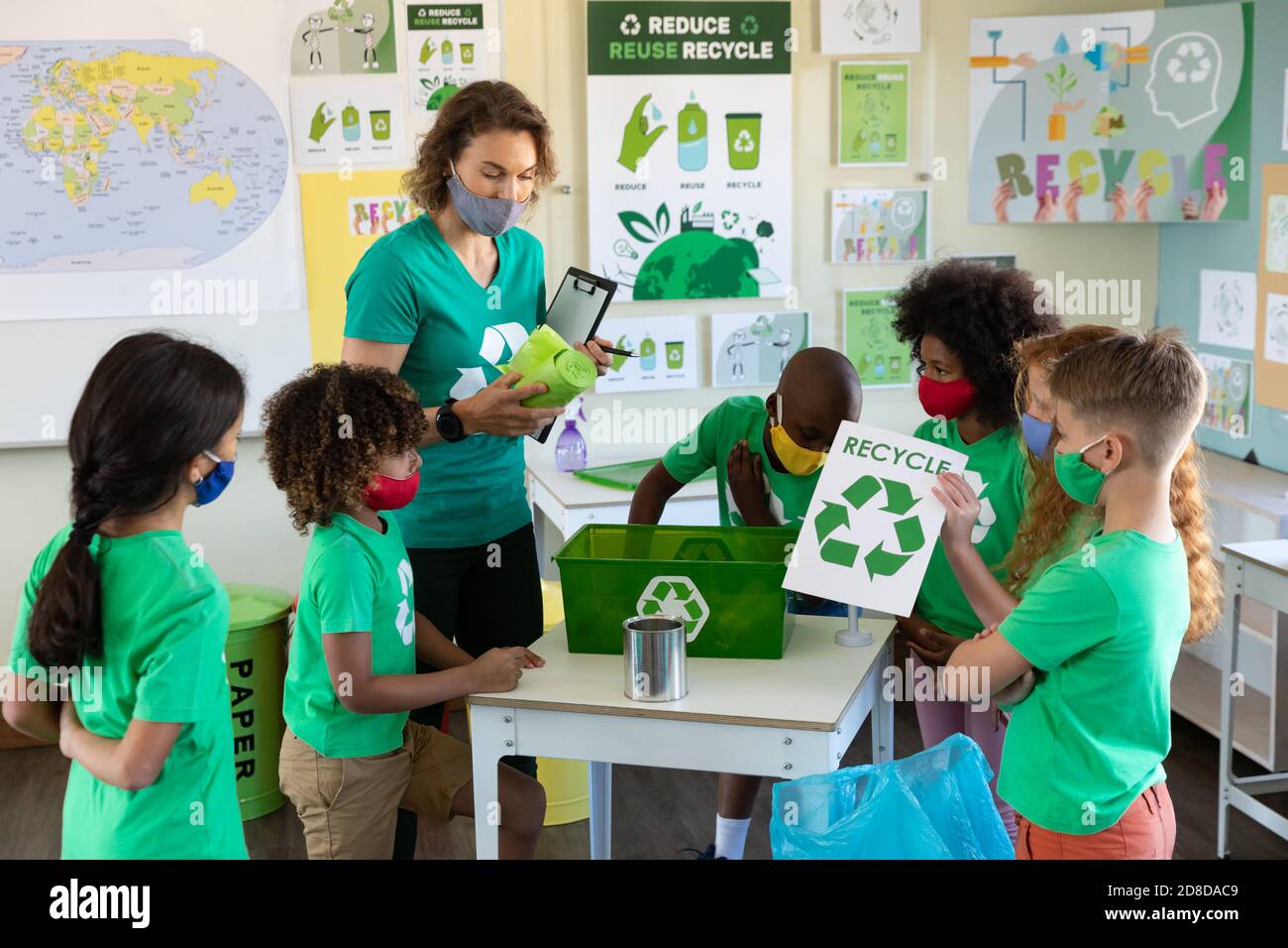 Female teacher and students wearing face masks with recycling container ...