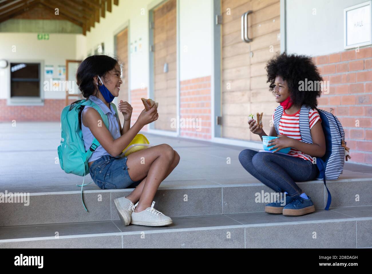 Two girls eating lunch from tiffin box while sitting on stairs at ...