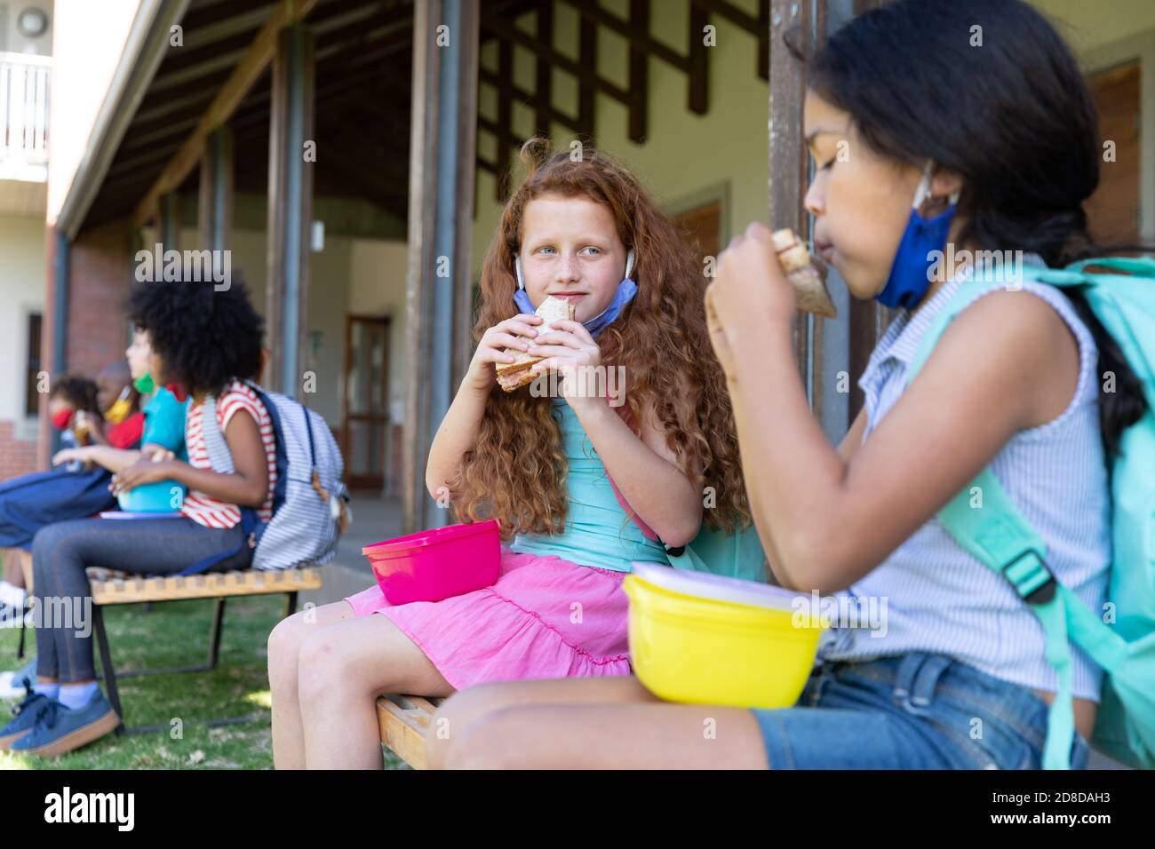 Two girls eating lunch from tiffin box while sitting on bench in the ...