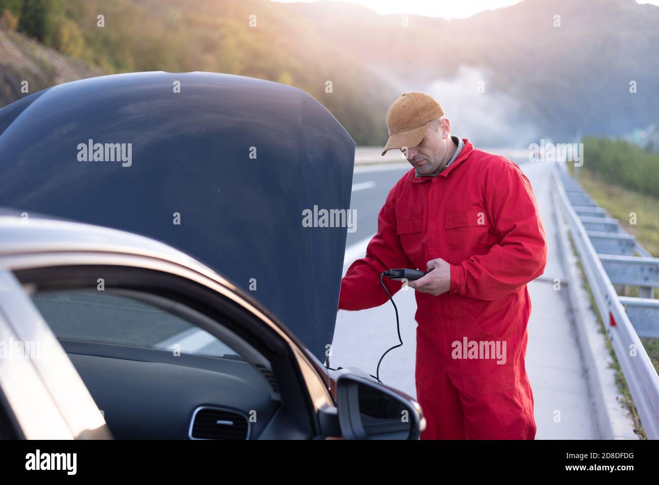 Handsome auto mechanic or road assistance worker in uniform repairing ...