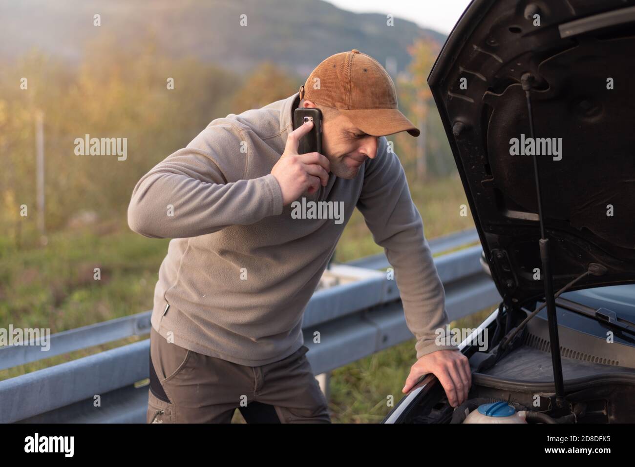 Angry young man waiting a help while sitting near the broken car at the ...