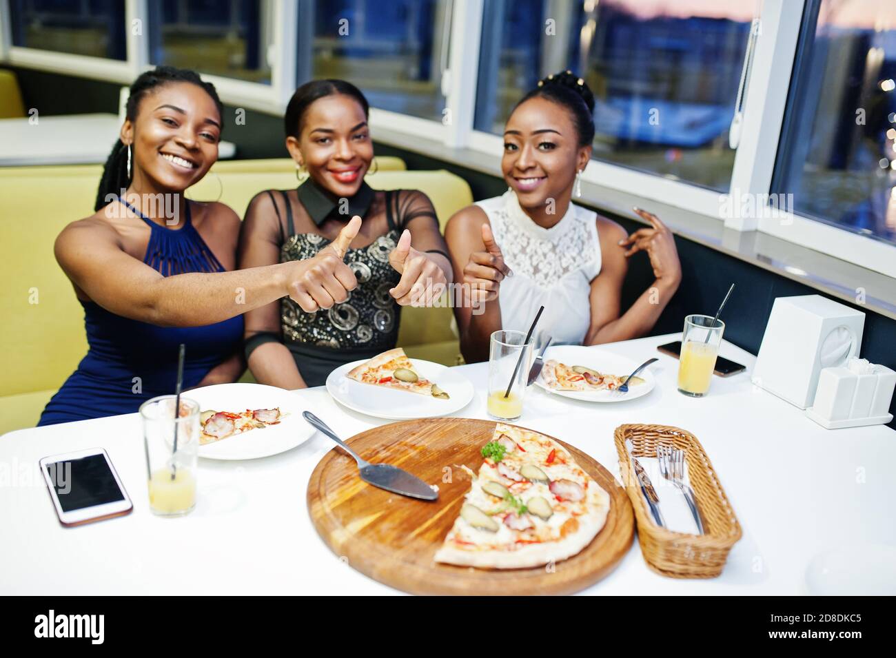 Three african woman in dress posing at restaurant, eating pizza and ...