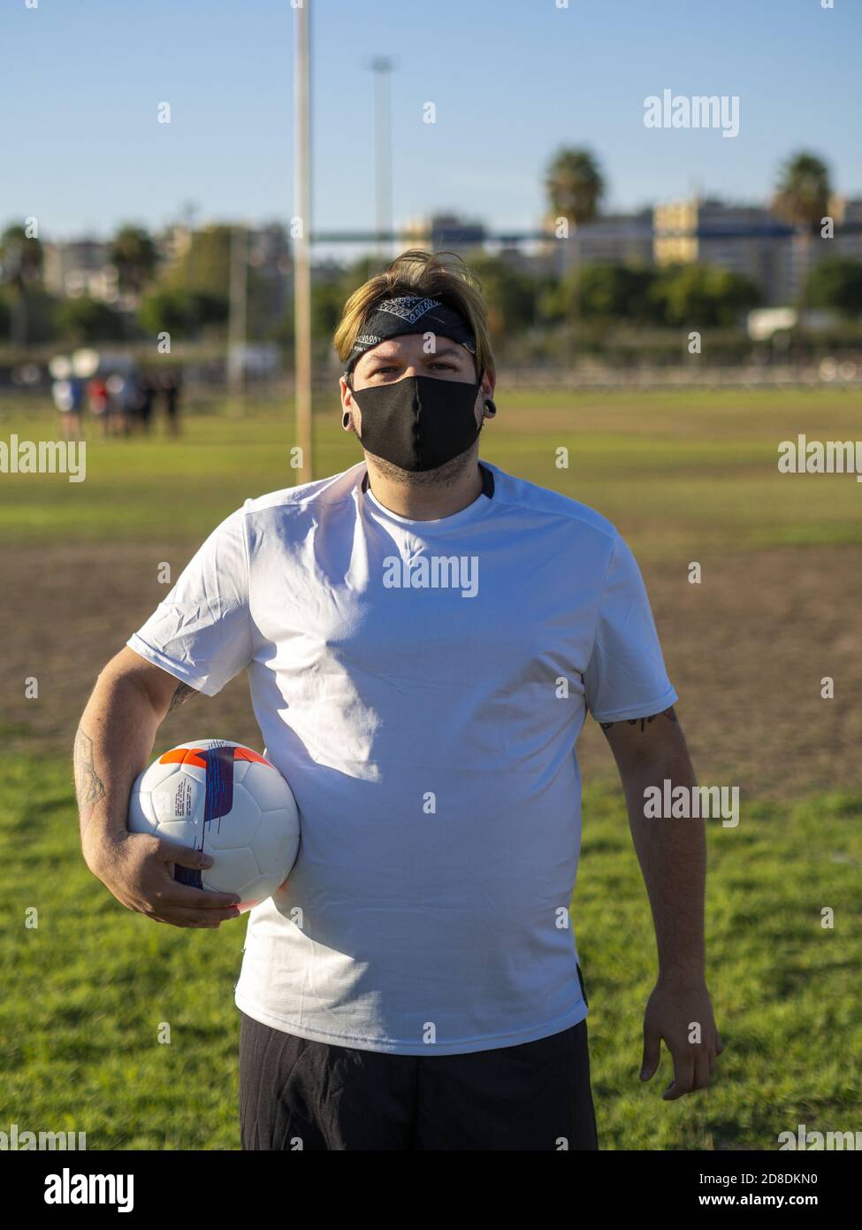 Young athlete with a white shirt and black mask holding a football ball ...