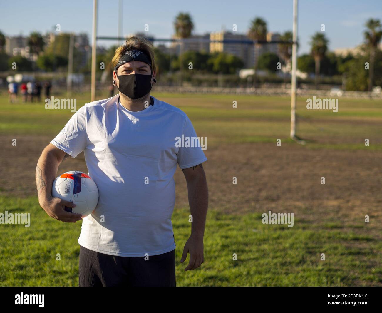 Young athlete with a white shirt and black mask holding a football ball ...