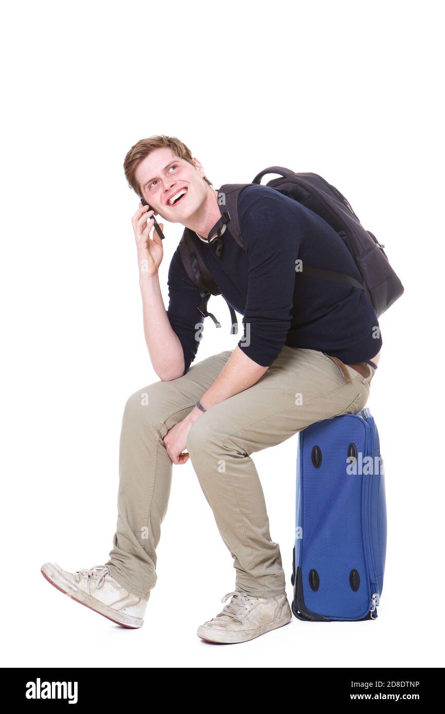Full body portrait of happy young man sitting on suitcase and talking ...