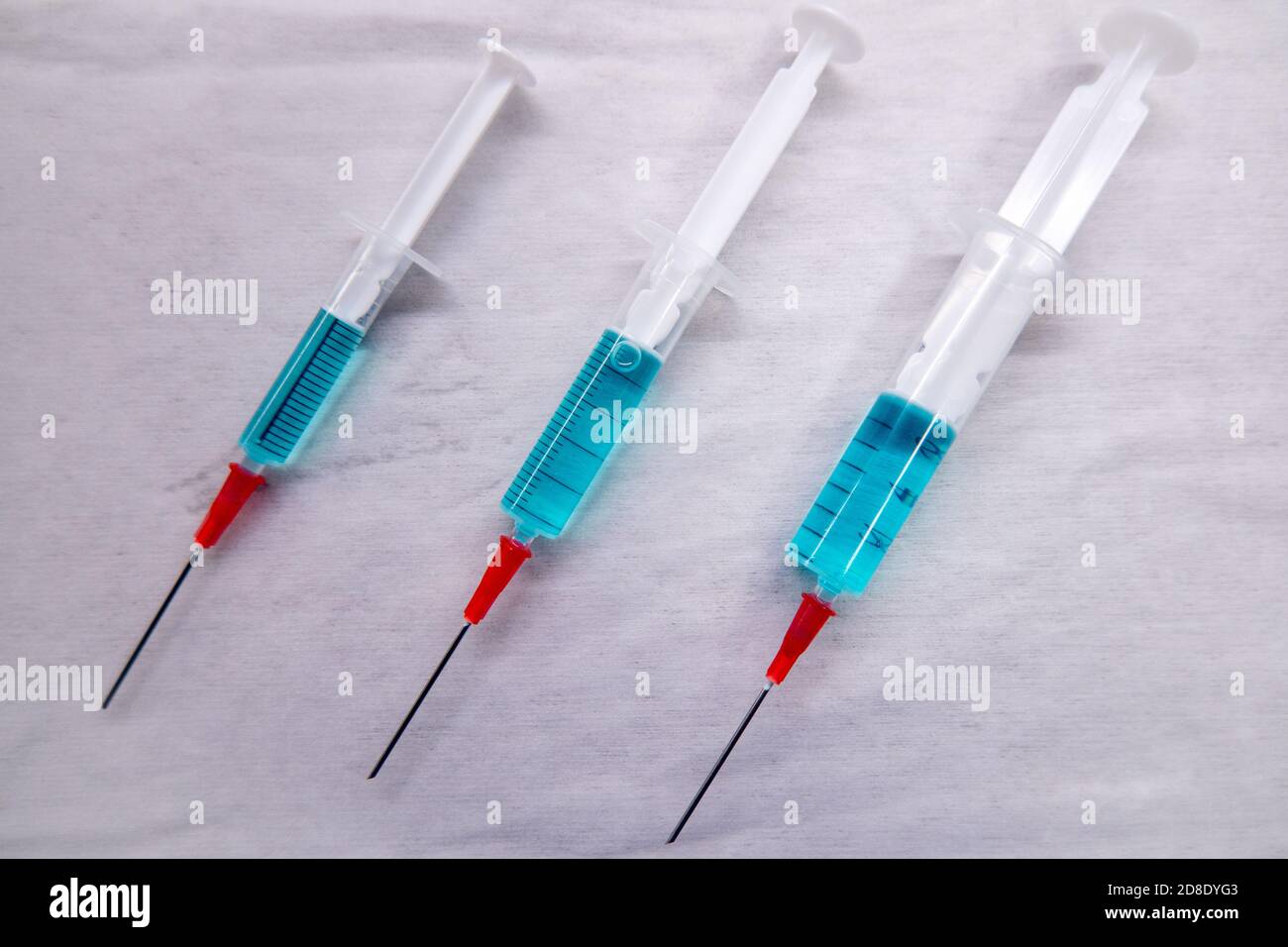 three differently sized syringes filled with blue liquid lie on a white ...