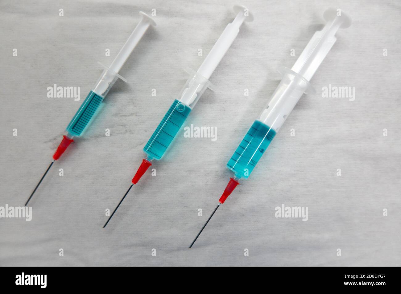 three differently sized syringes filled with blue liquid lie on a white ...
