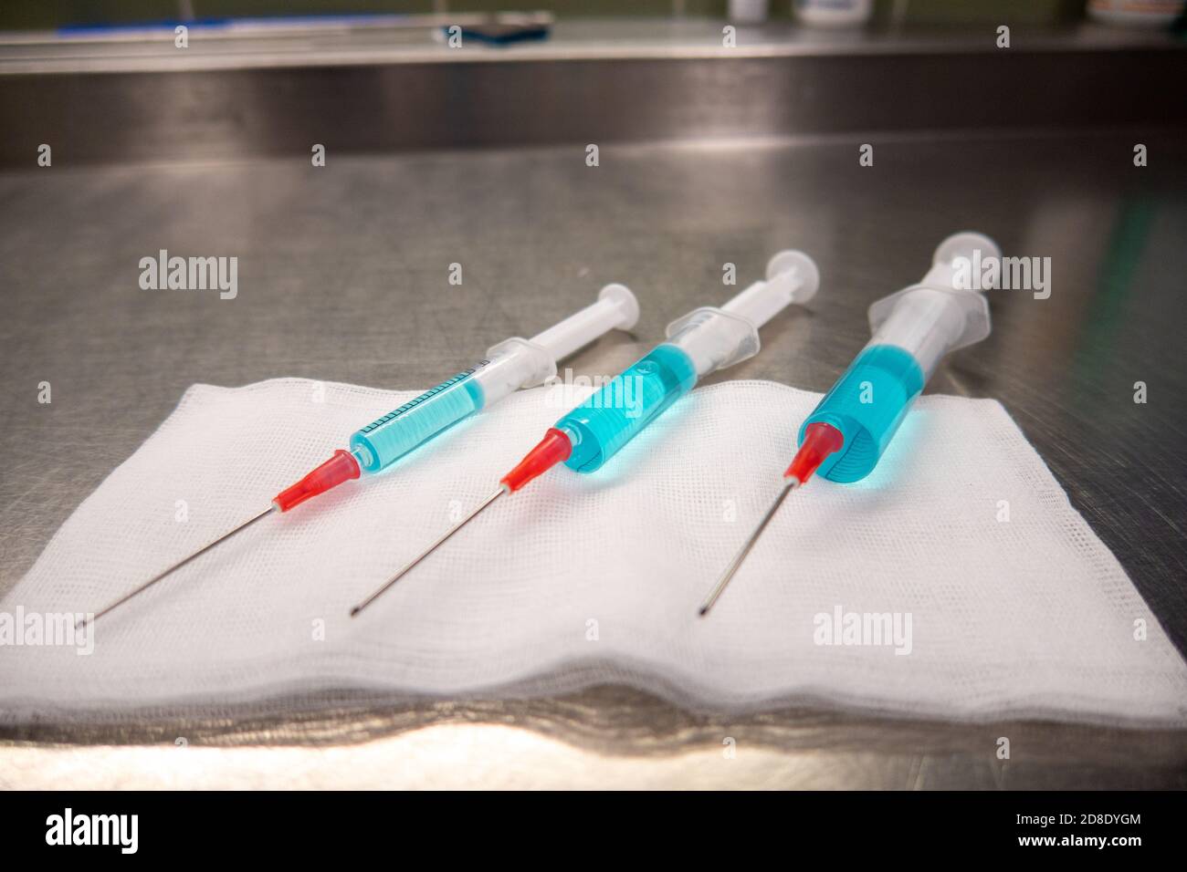 three differently sized syringes filled with blue liquid lie on a white ...