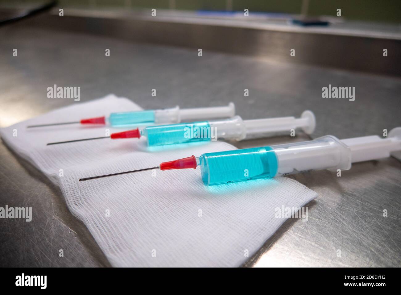 three differently sized syringes filled with blue liquid lie on a white ...