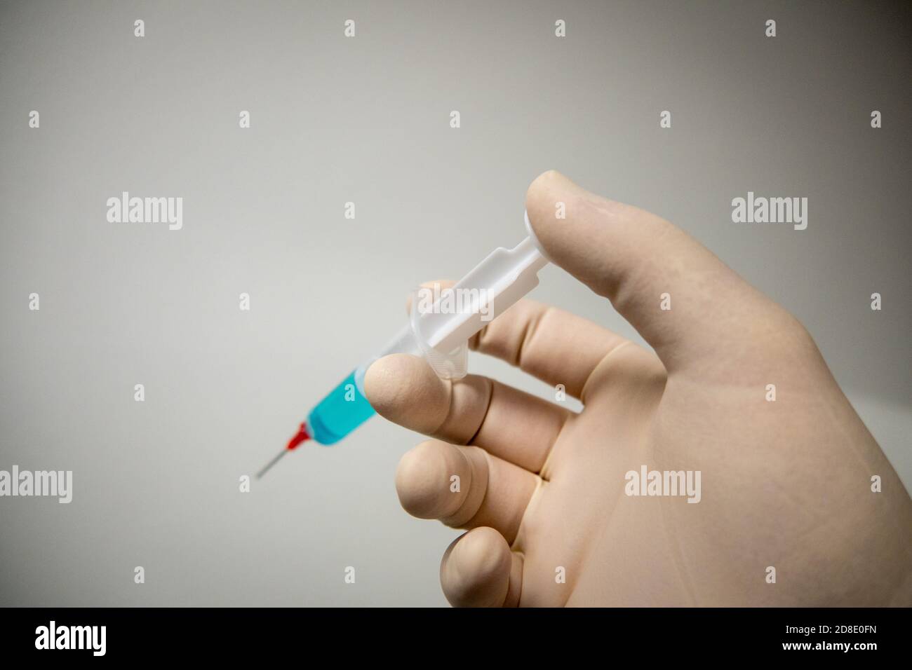one hand with a glove holds a medical syringe with blue liquid Stock ...
