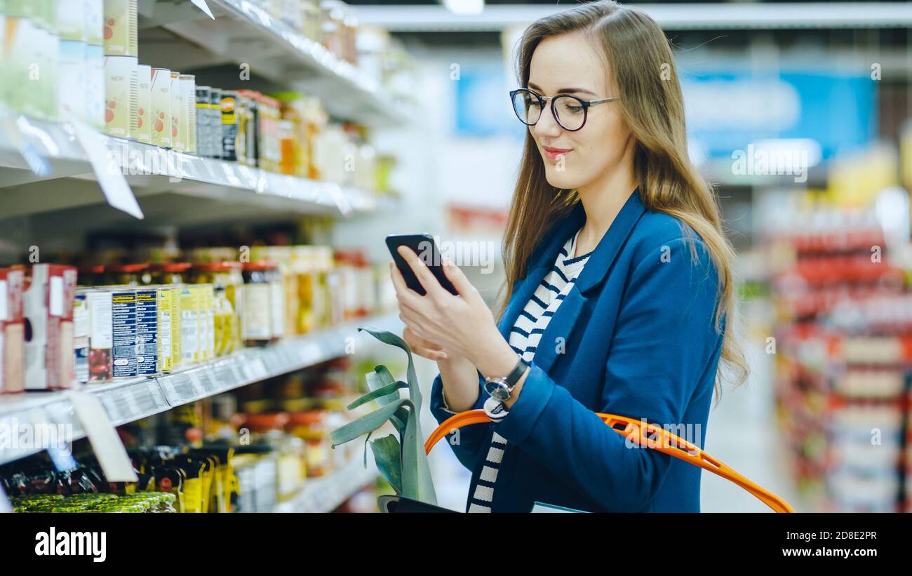 At the Supermarket: Beautiful Young Woman Uses Smartphone While ...