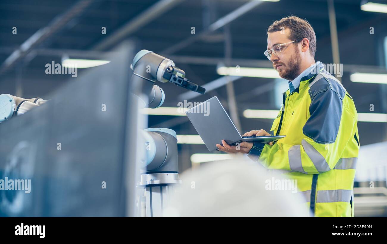 At the Factory: Automation Engineer Uses Laptop for Programming Robotic ...