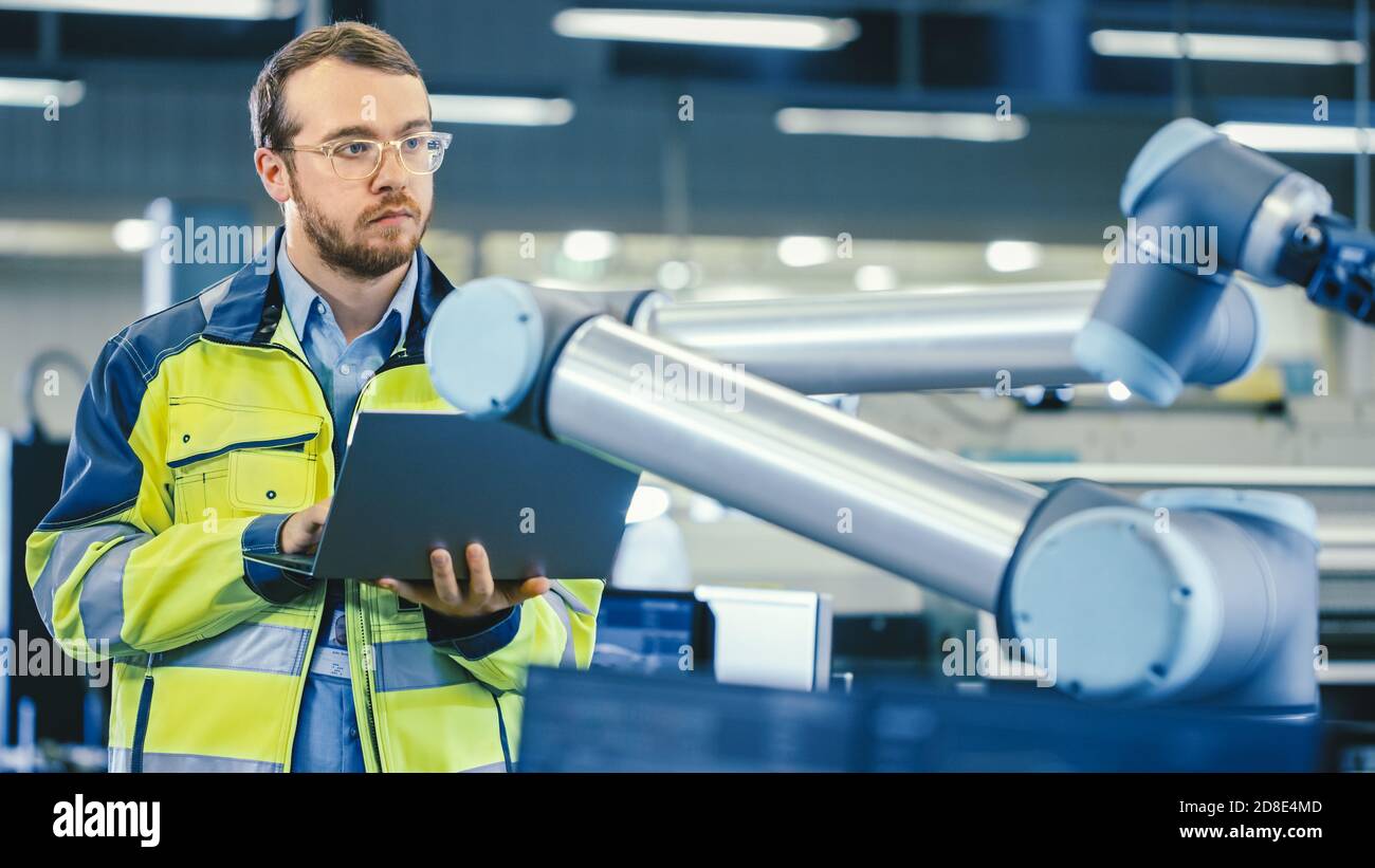 At the Factory: Automation Engineer Uses Laptop for Programming Robotic ...
