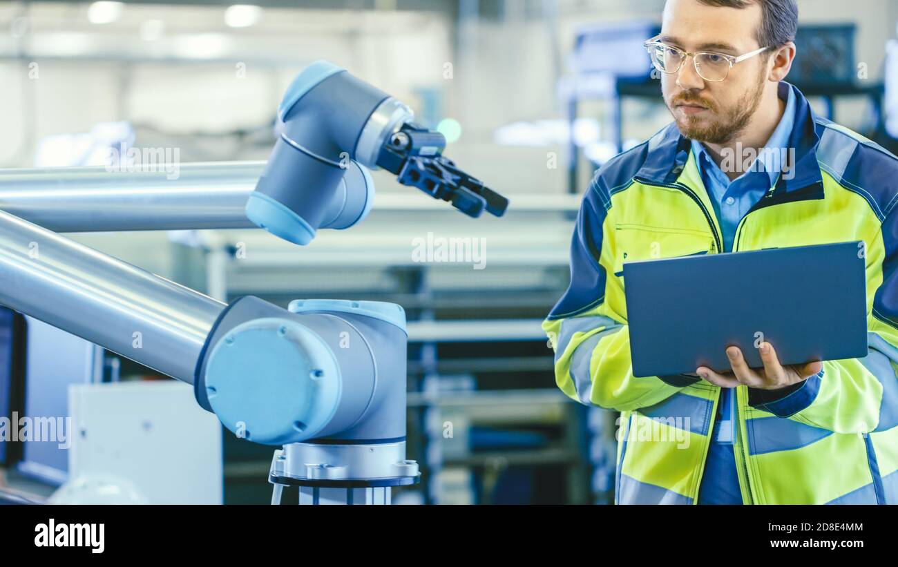 At the Factory: Automation Engineer Uses Laptop for Programming Robotic ...