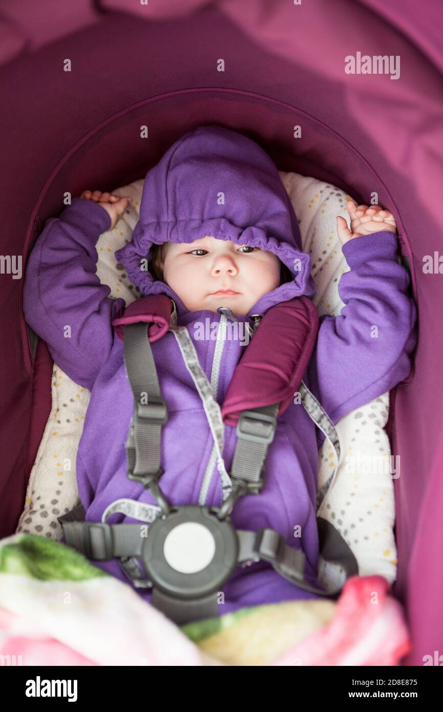 Caucasian baby boy lying inside of pram with hands up, fastened with ...