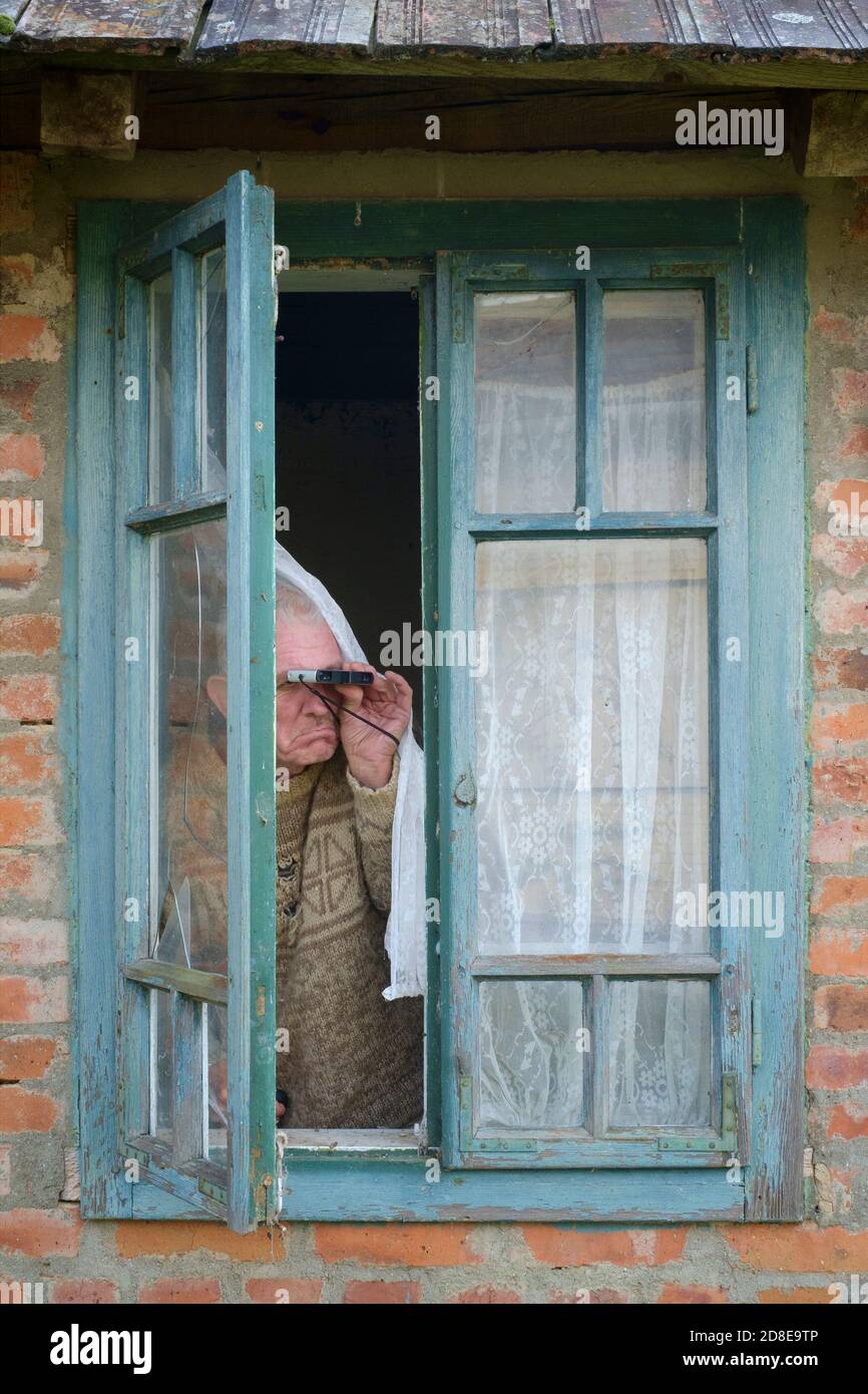 miserable looking older male curtain twitcher spying on neighbours from ...