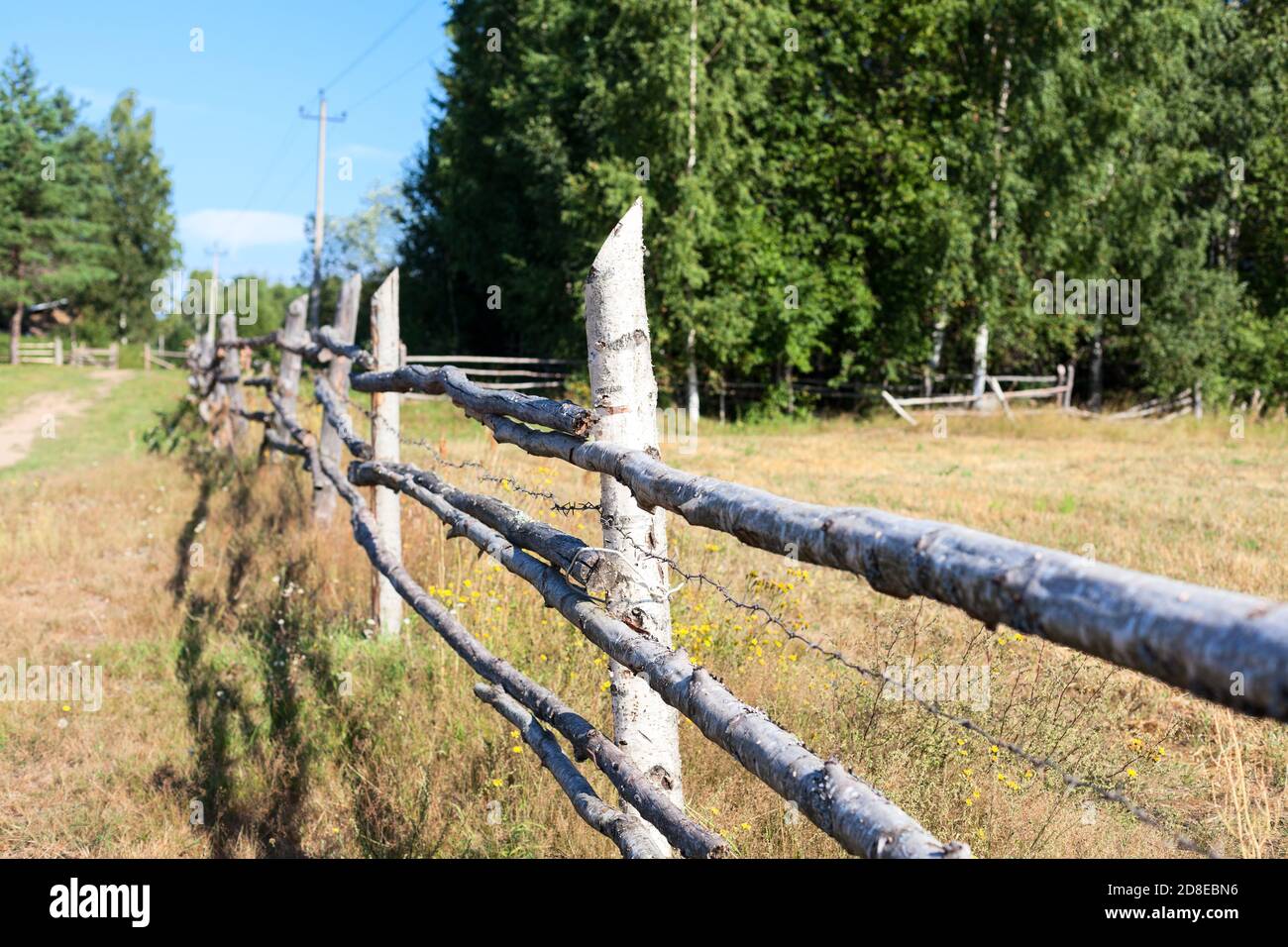 Rural wooden fence with barbed wire, dry grass is on a field at summer ...