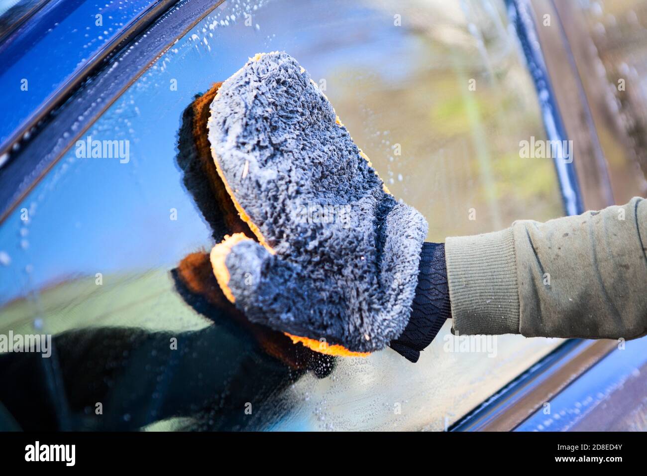 Human hand wearing microfiber mitten washes a car window with water and ...