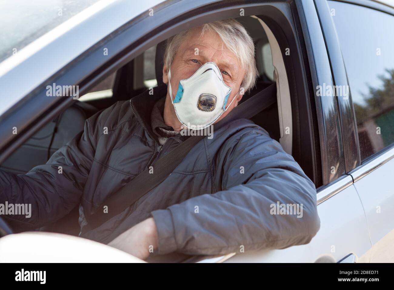 Retirement age Caucasian man driving a car wearing dust face mask ...