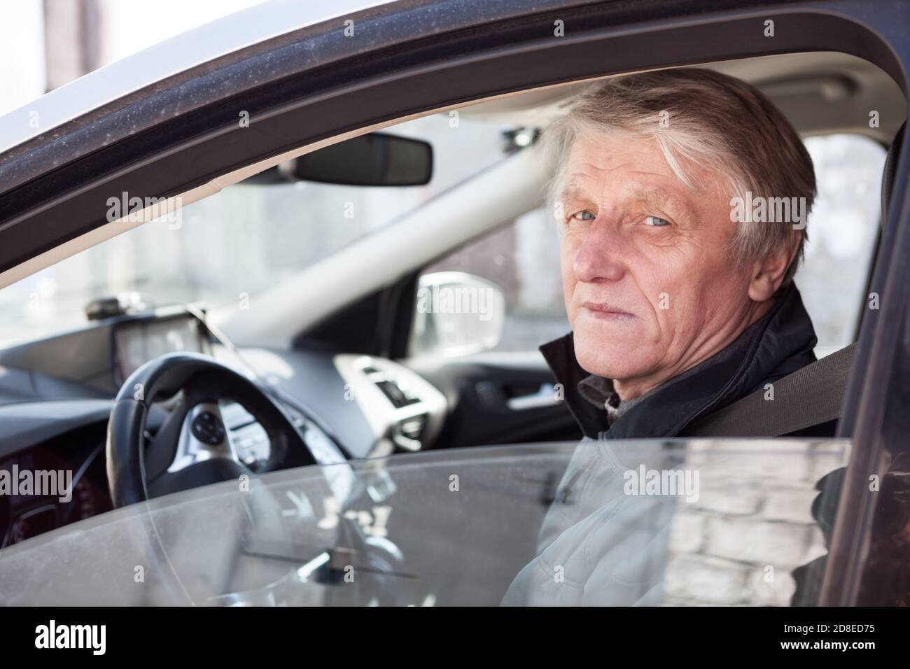 Senior Caucasian man a driver sitting inside the car with severe look ...