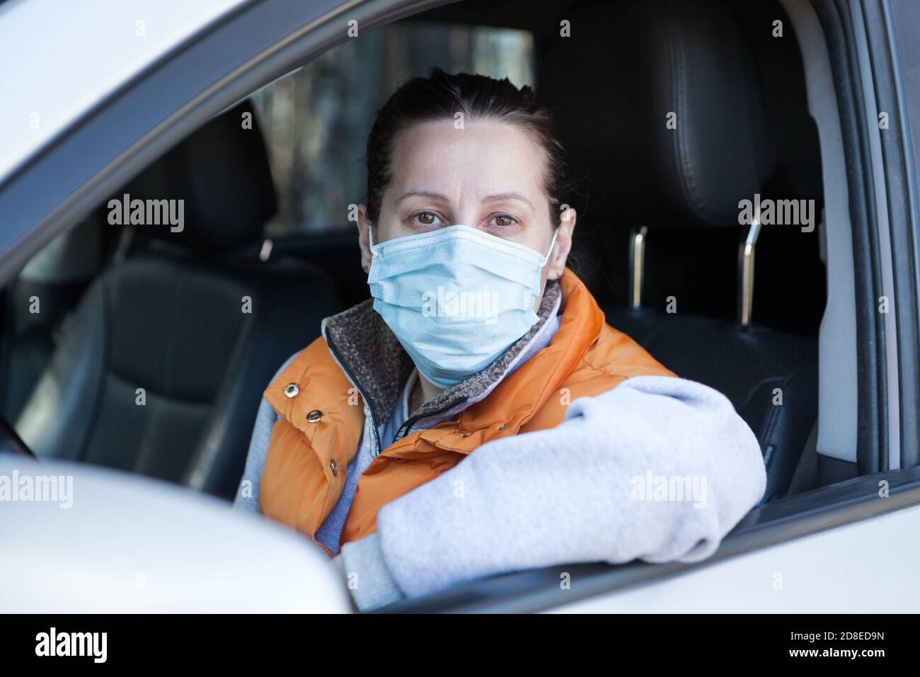Young woman is ready to drive a car with protective mask on her face ...