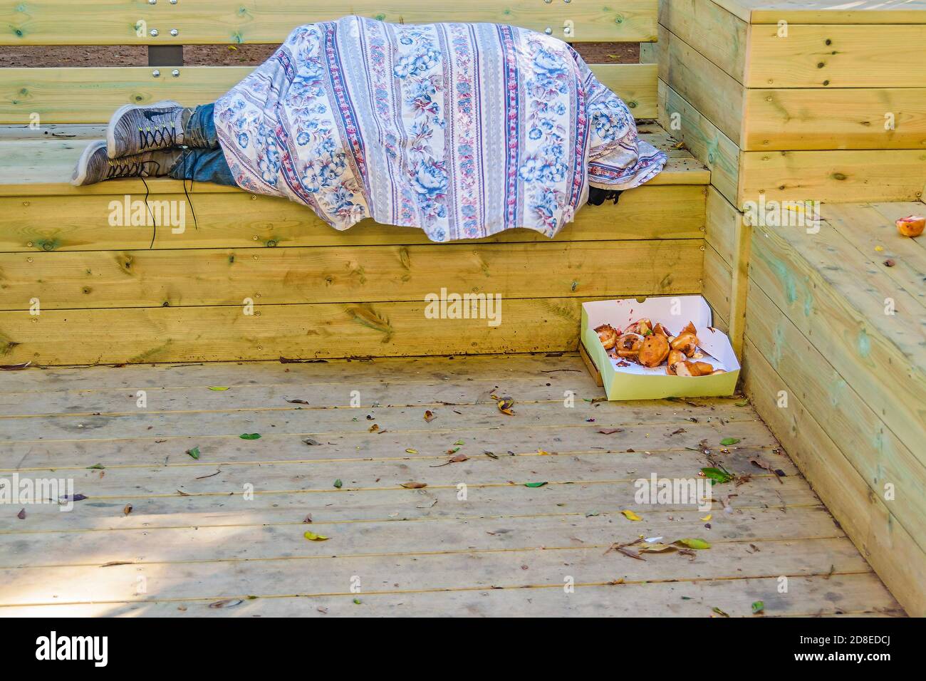 Homeless covering with a blanket sleeping at wooden seat park, tel aviv ...