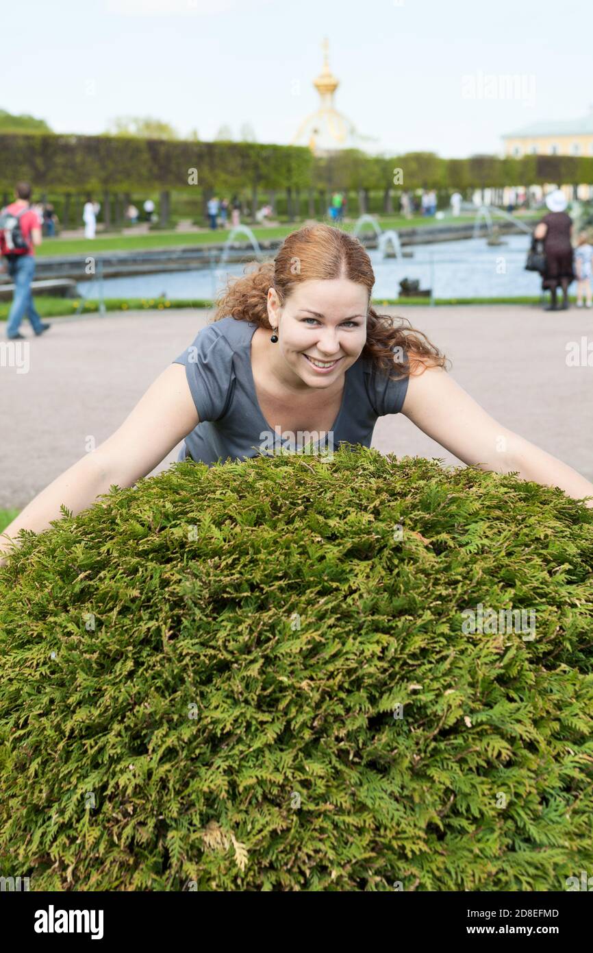 Portrait of happy Caucasian woman trying to embrace green bush in an ...