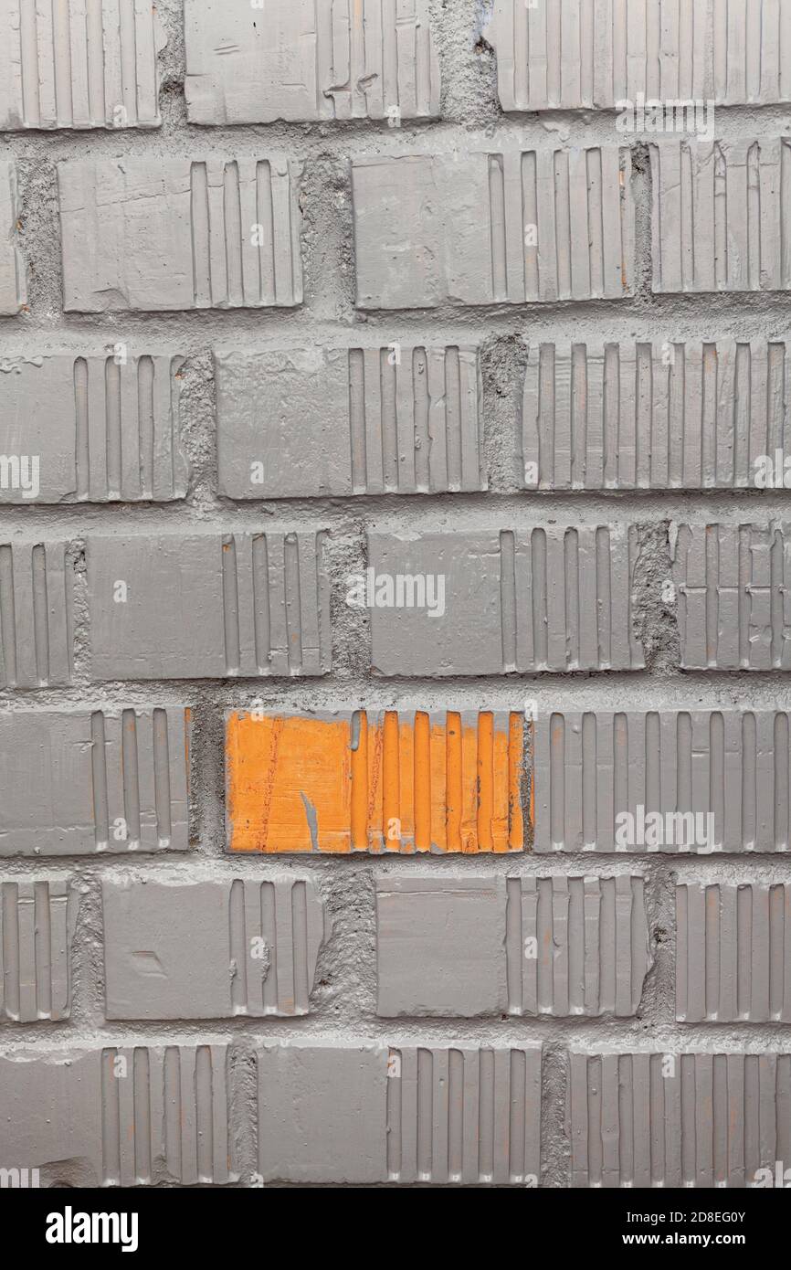 Unpainted brick of wall, one orange rectangle between grey blocks, a ...