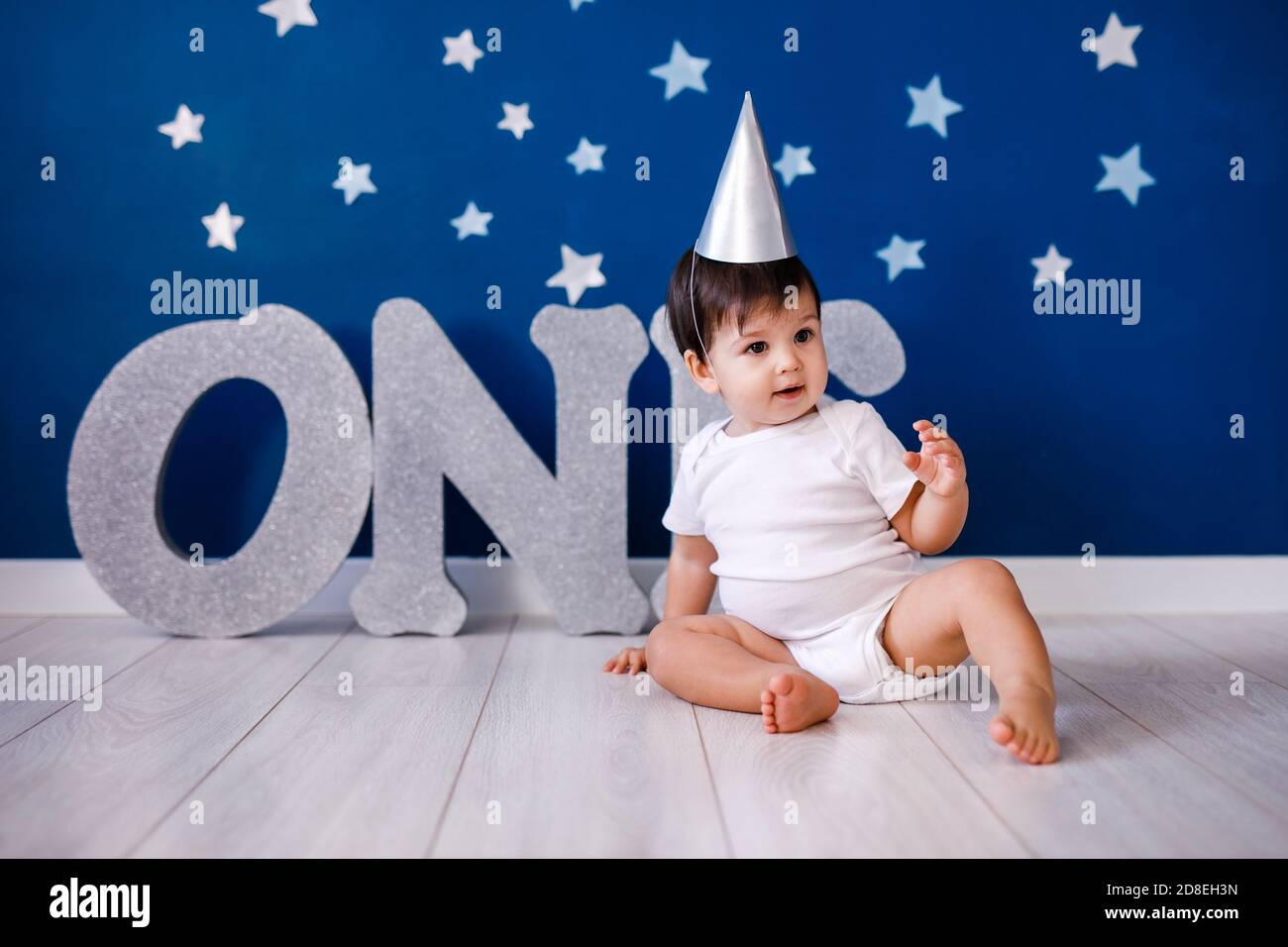 One year old baby boy in white t-shirt and silver hat celebrates ...