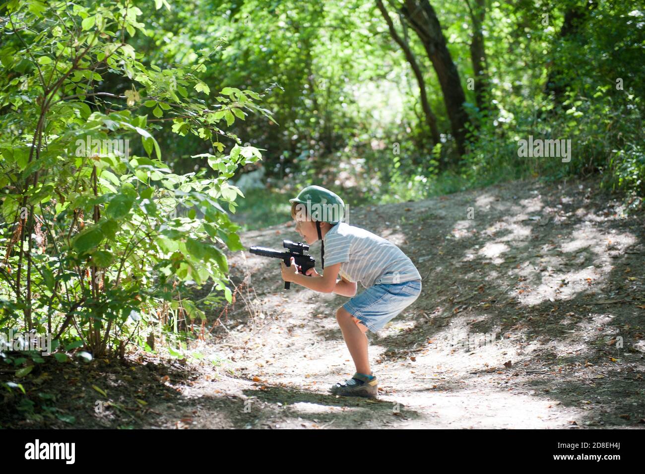 funny little boy in military helmet hiding behind trees with toy gun in ...