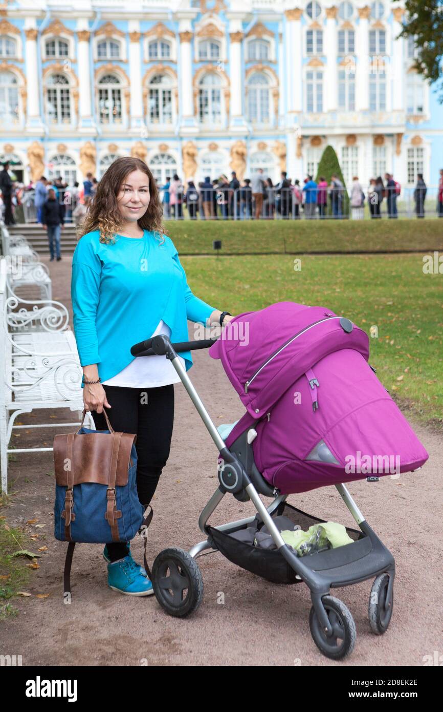 Young mother with stroller walking in summer park near palace ...