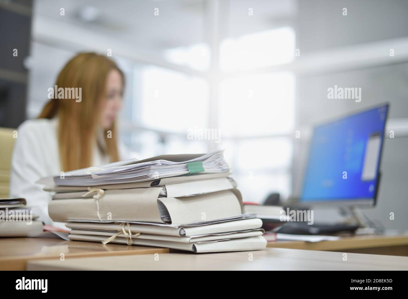 A large stack of papers in the office lies on the desk of a busy woman ...