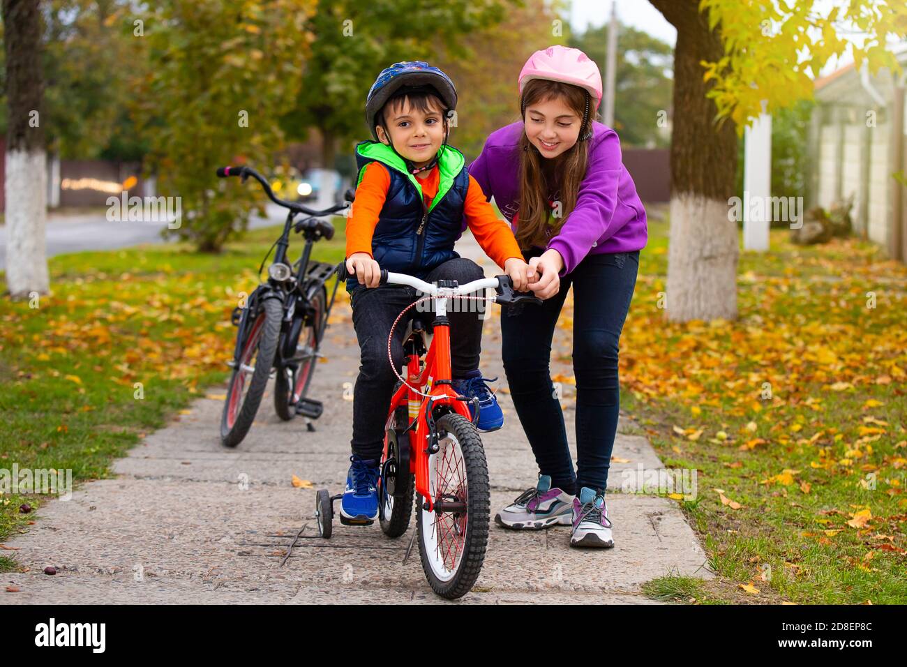 A sister teaches her little brother to ride a bike in an autumn park in ...