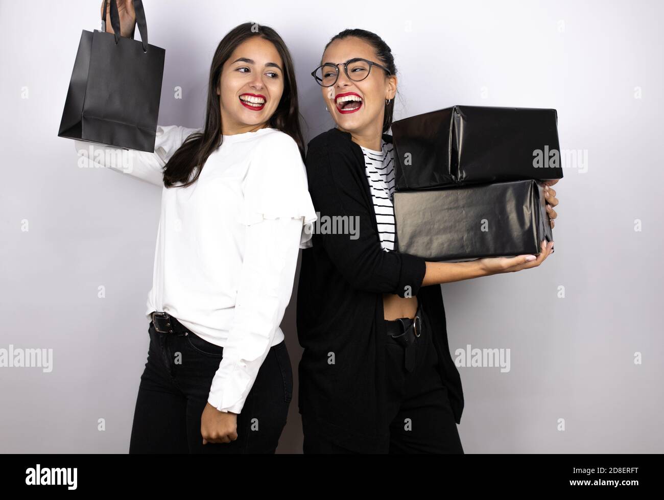 two young beautiful women holding black shopping bags and boxes smiling ...