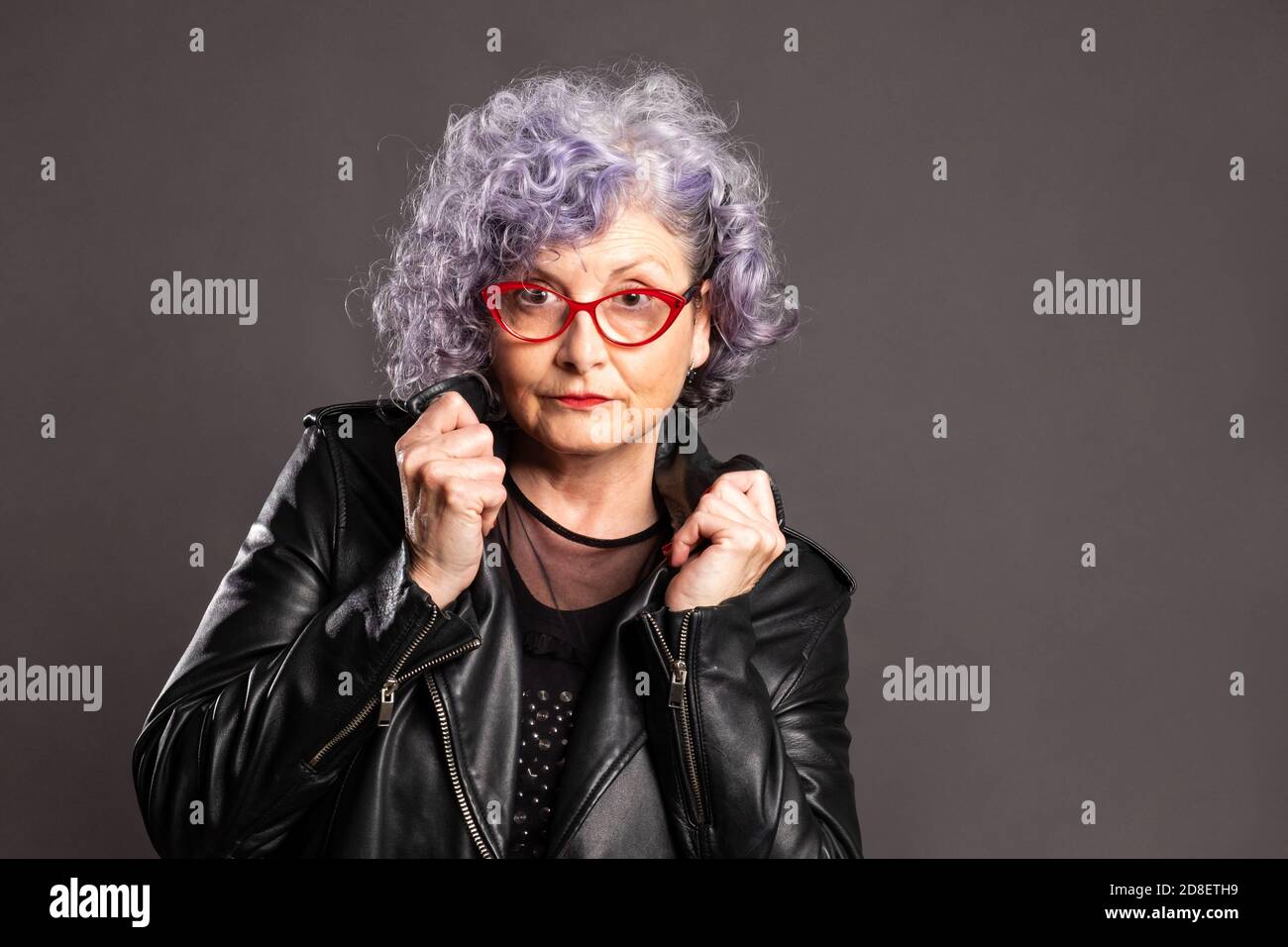portrait of beautiful old woman wearing leather jacket on a gray ...