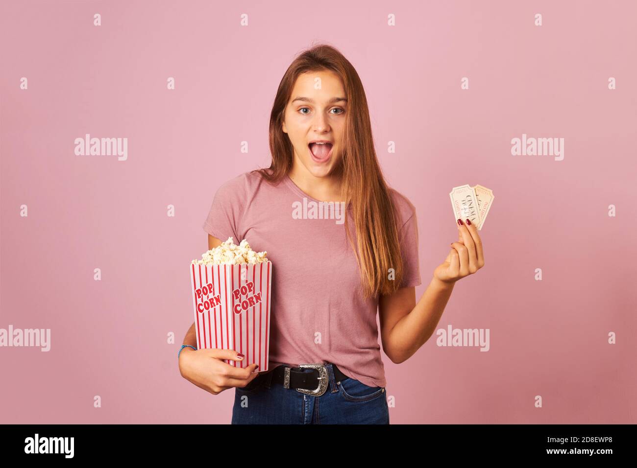 young beautiful woman holding popcorn and cinema tickets on a pink ...