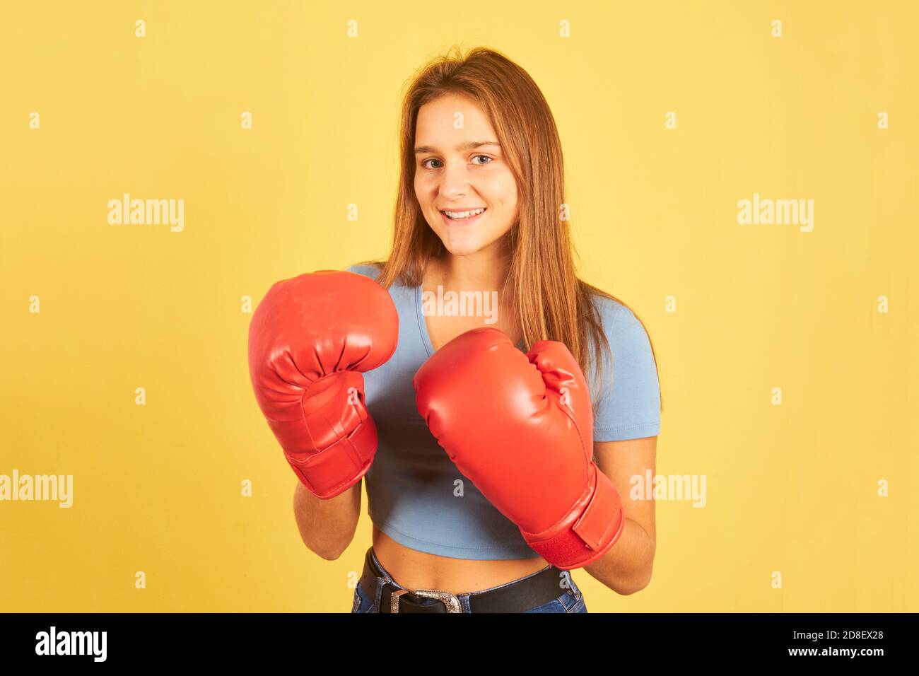 Portrait of young fighter woman wearing red boxing gloves on yellow ...