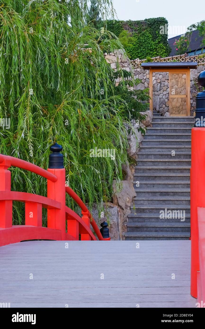 Arched wooden red footbridge and stone steps of stairway leading up to ...