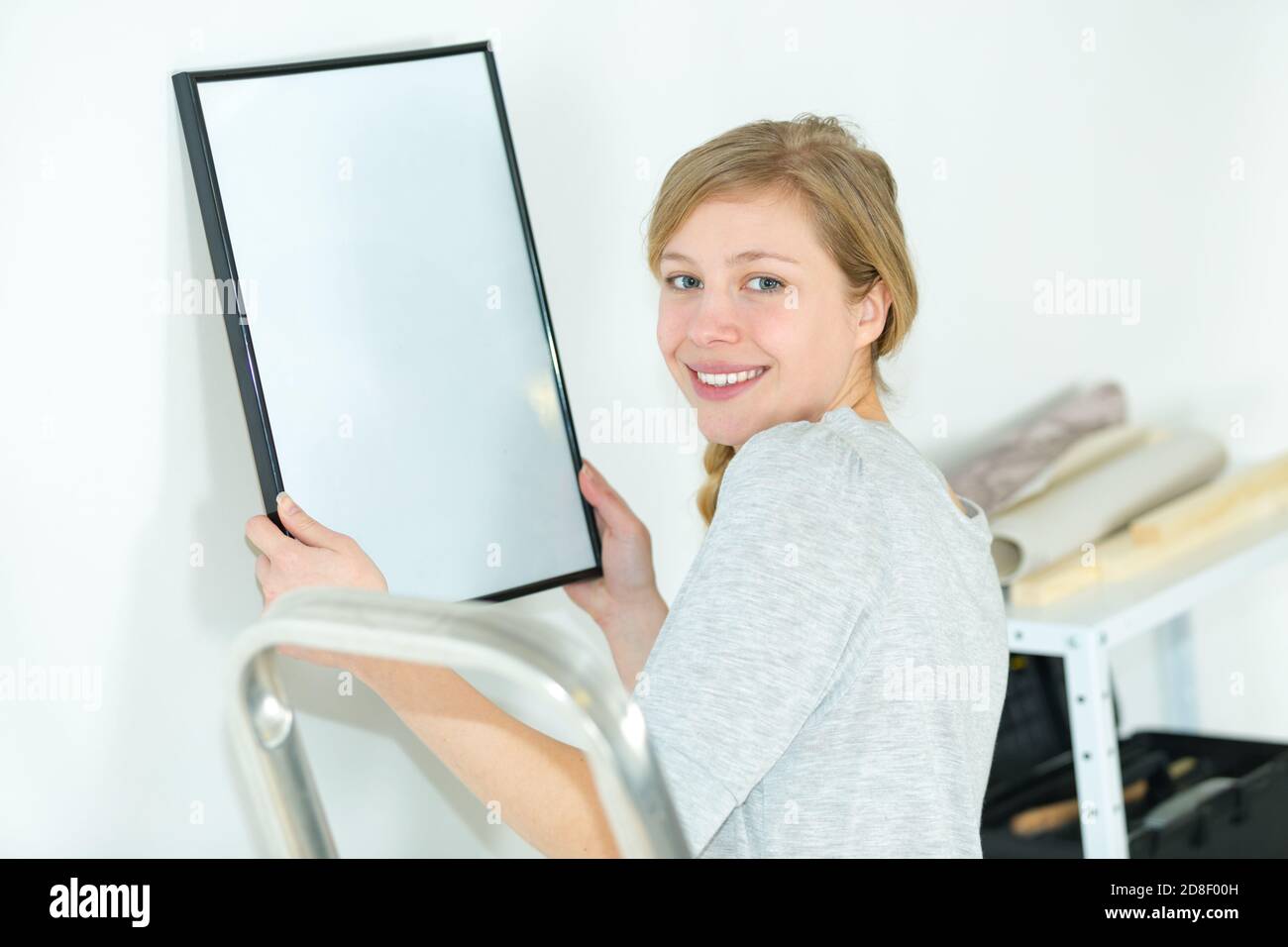 woman hanging picture frame on wall in new house Stock Photo - Alamy