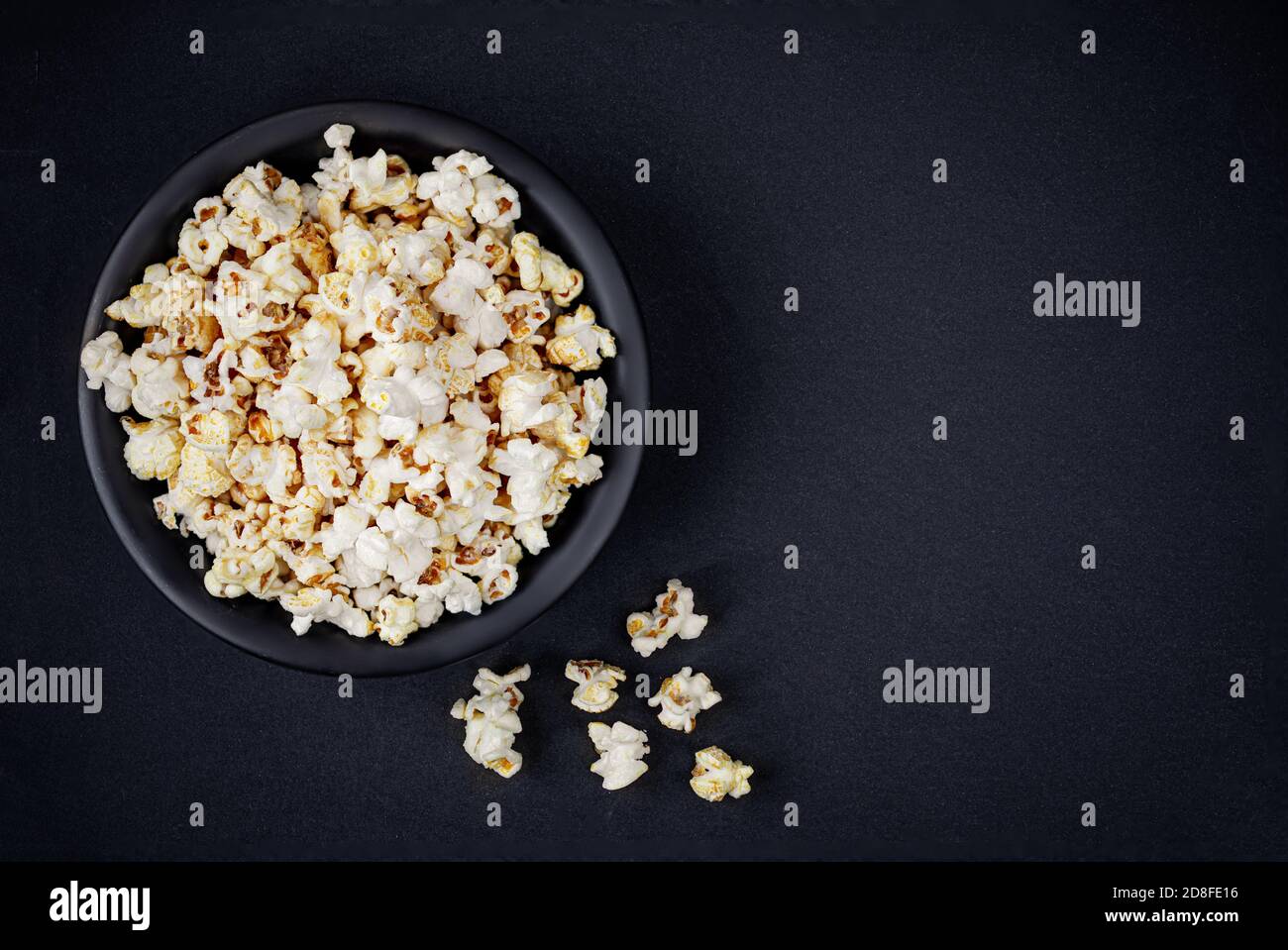 Scattered salted popcorn in a bowl on black background with copy space ...