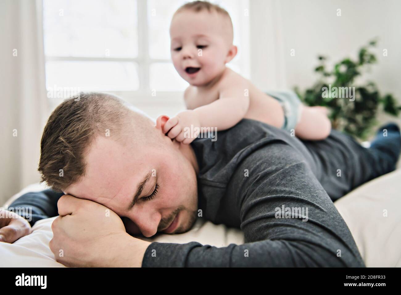 Tired father sleep but his baby boy interferes him. Young happy father ...