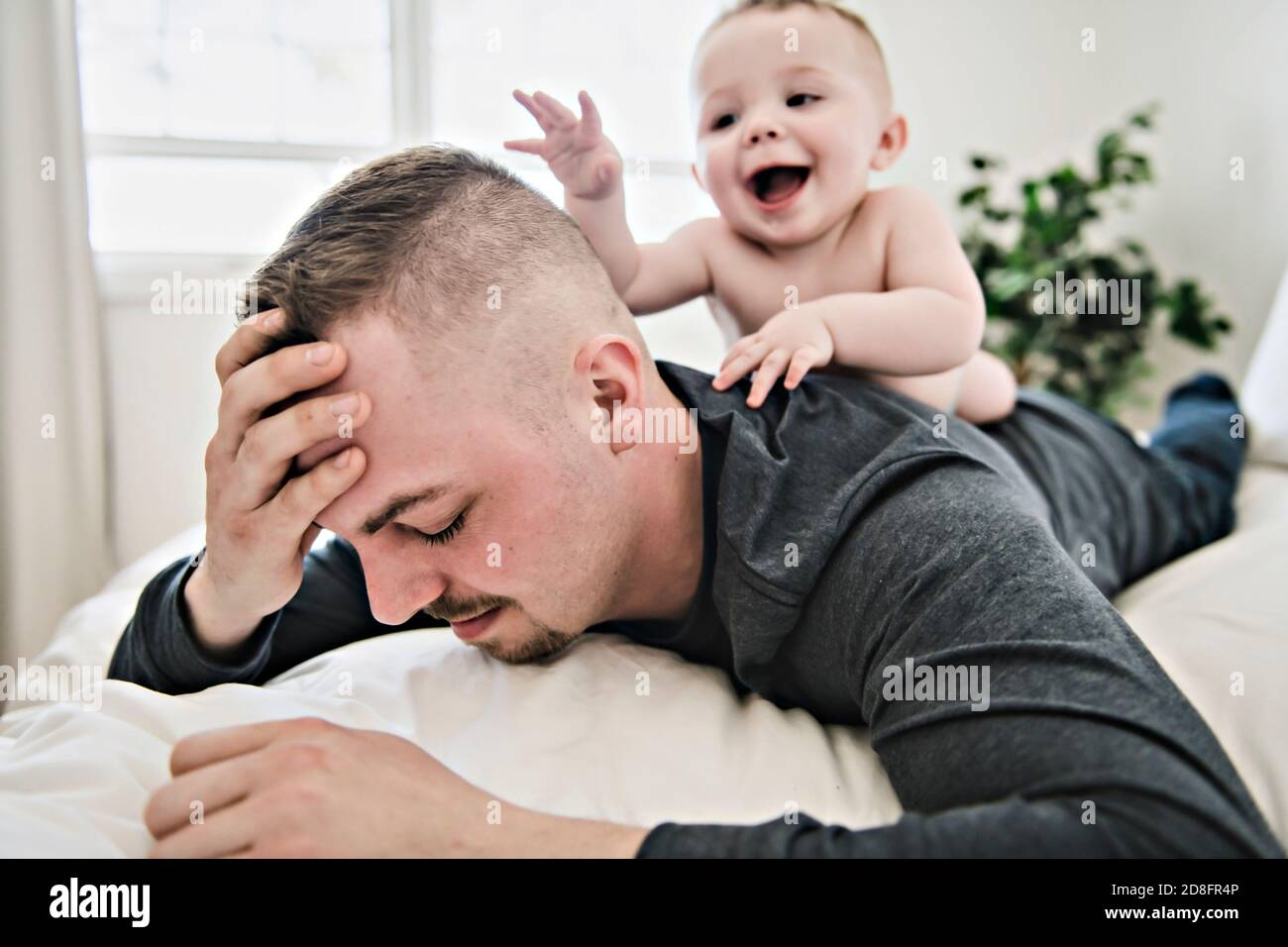 Tired father sleep but his baby boy interferes him. Young happy father ...