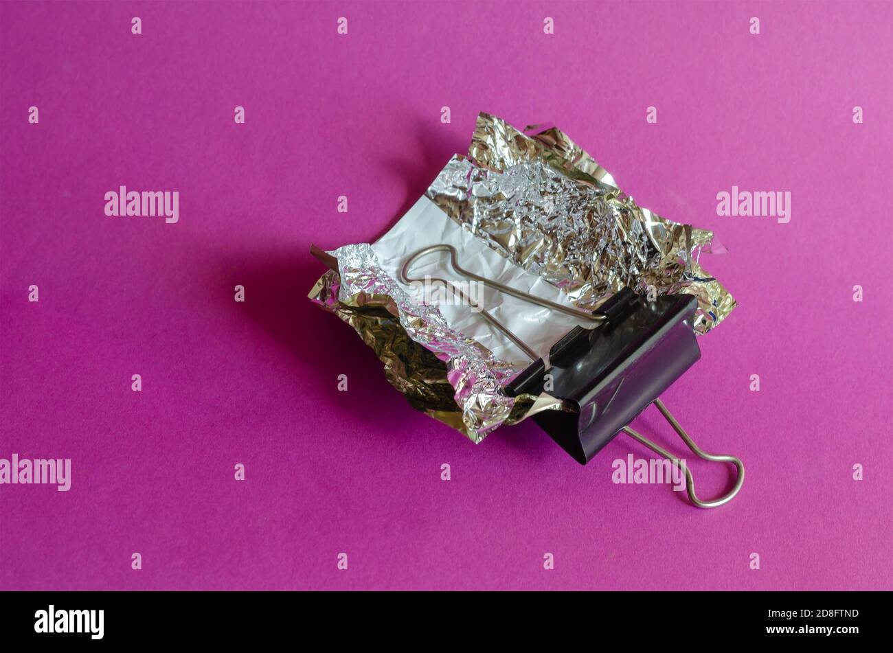 Smashed candy wrappers and Metal black Binder Clip on purple background ...