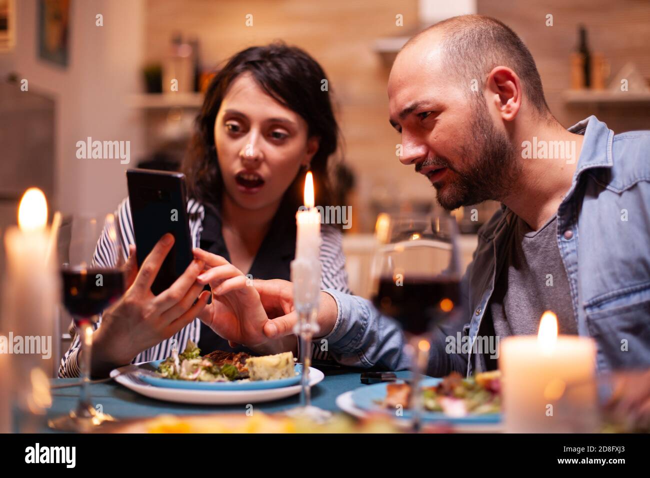 Husband and wife looking shocked at phone while having romantic dinner ...
