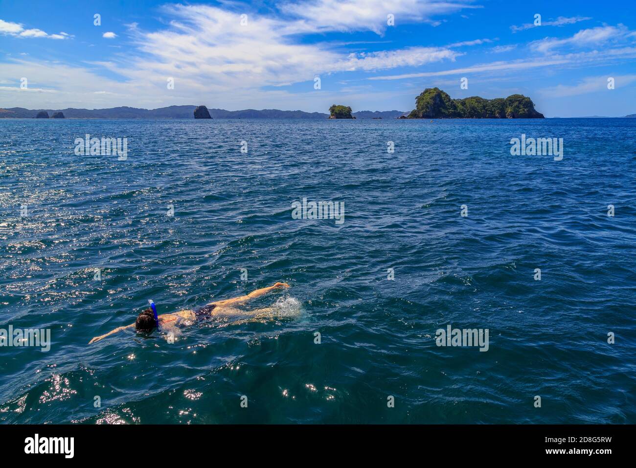 A woman snorkeling in the deep blue ocean, with small islands in the ...