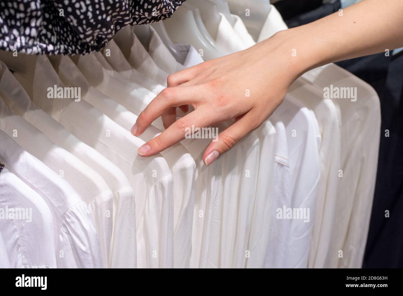 girl chooses a white shirt in the store. Selection of new clothes close ...