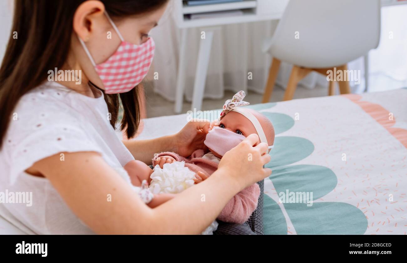 Girl with mask putting small mask on her doll Stock Photo - Alamy