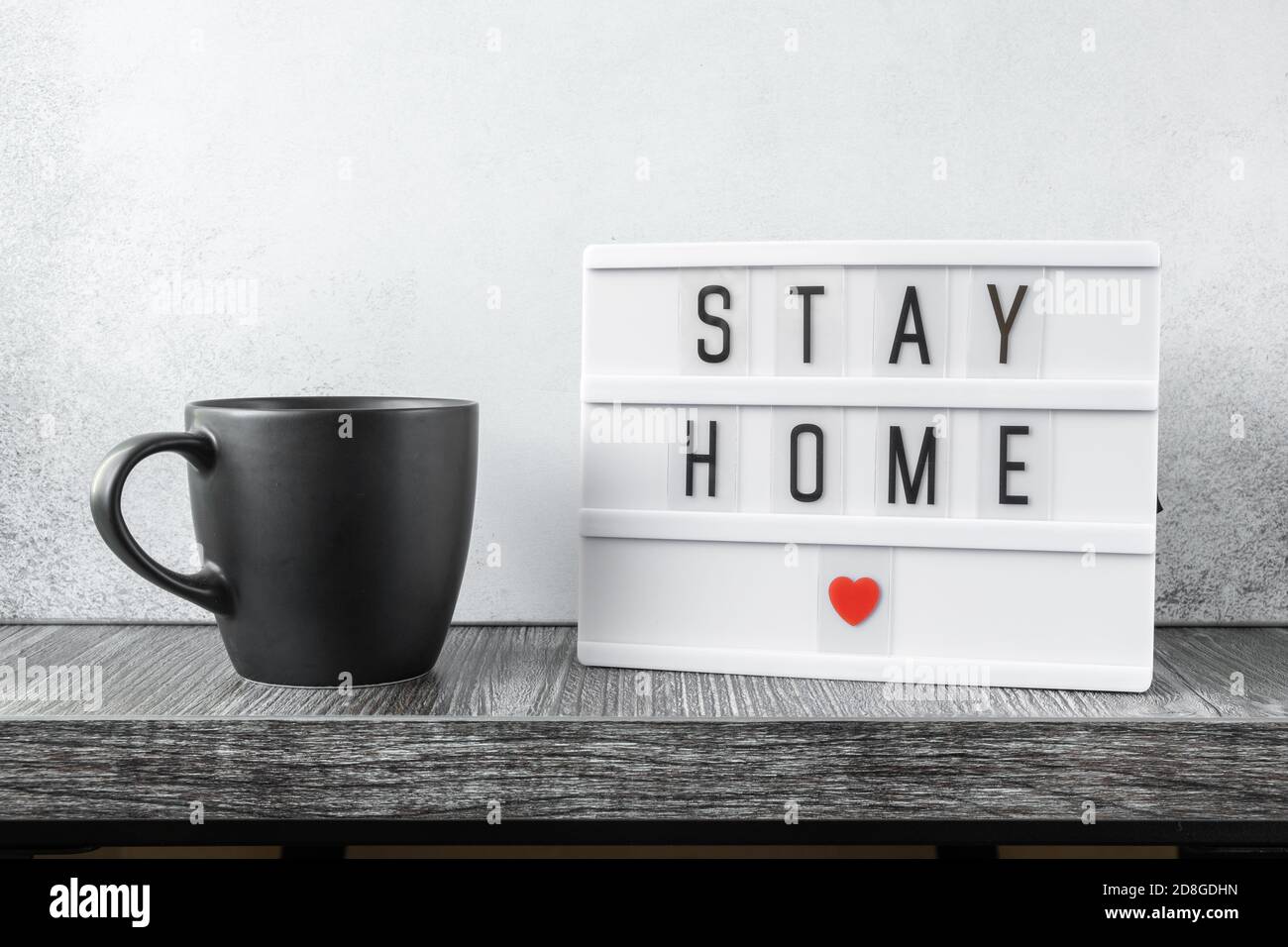 Lightbox with text STAY HOME and black mug with tea or coffee on wooden ...