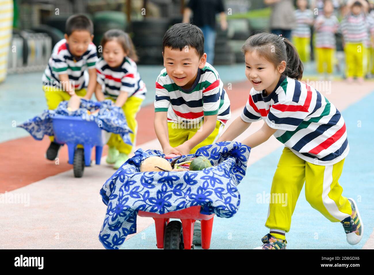 Kids play harvest competition by using a push cart filled with farm ...