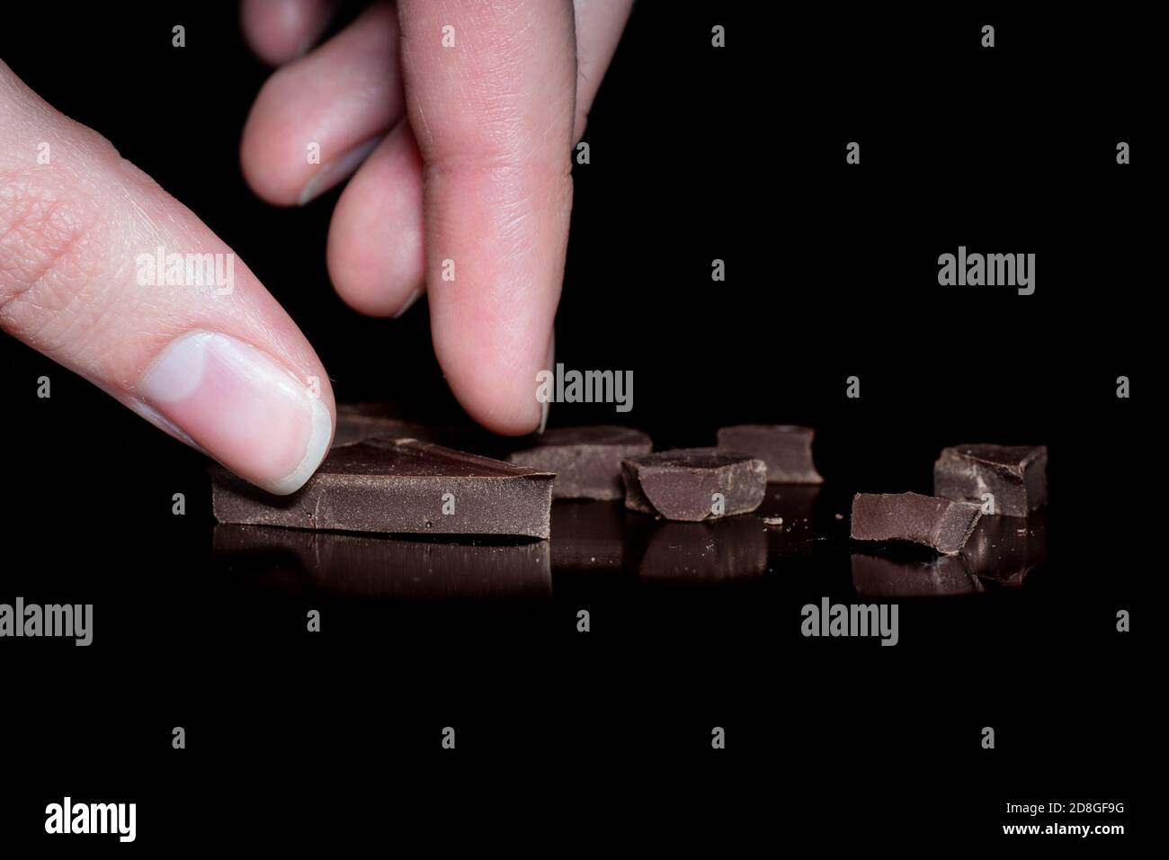 Close-up female hand takes pieces of black bitter chocolate isolated on ...